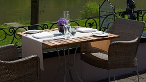 Uma área de refeições ao ar livre com uma mesa posta para dois, com vista para um lago tranquilo.