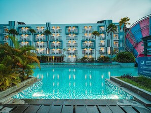 Um hotel com piscina, várias varandas e palmeiras.