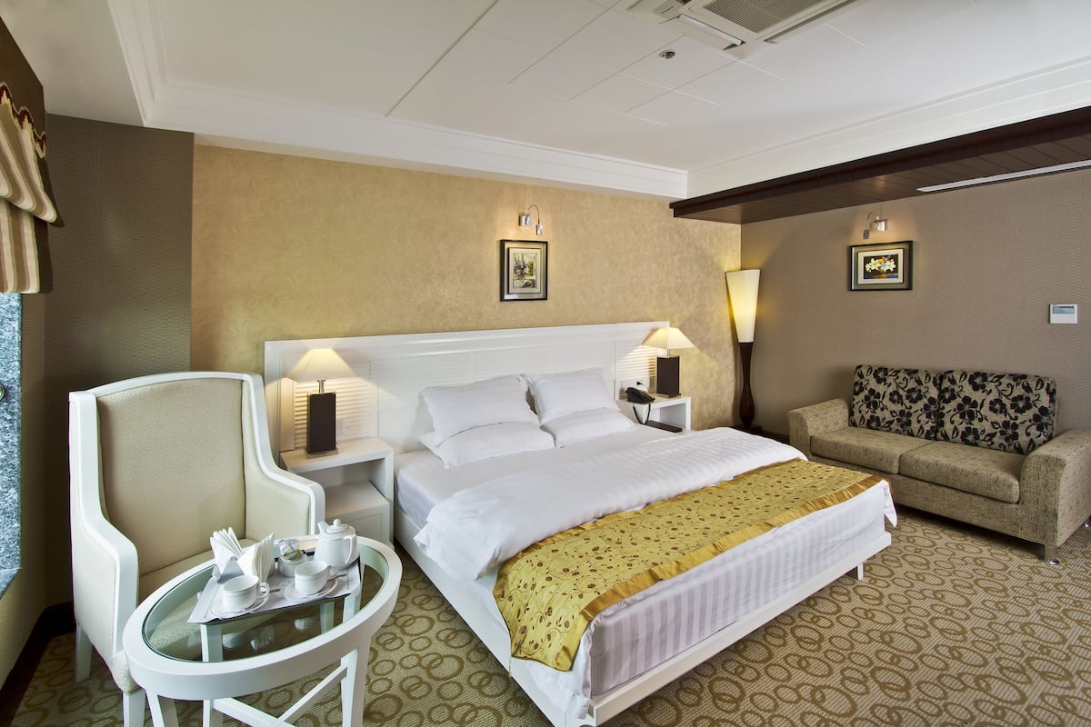 Quarto de hotel com cama, sofá, mesa pequena com bandeja de itens de café da manhã e duas luminárias fixadas na parede.