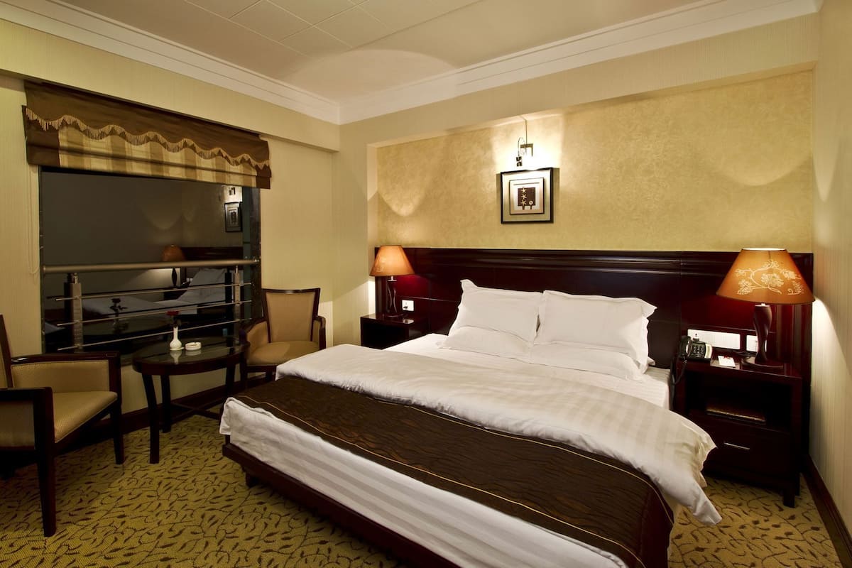 Quarto de hotel com uma cama grande, duas luminárias de cabeceira, uma escrivaninha com cadeira, televisão e um quadro na parede.