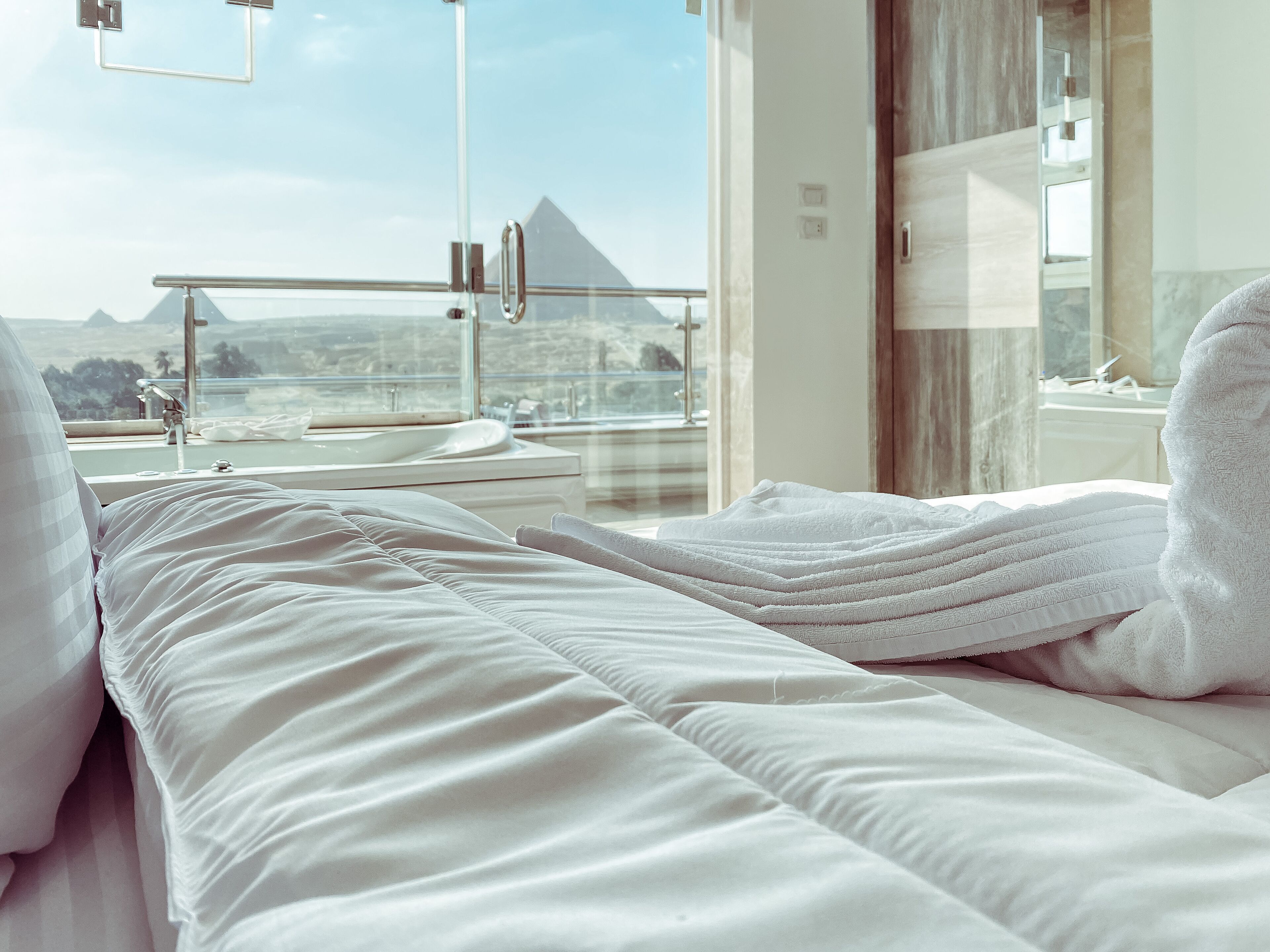 Quarto de hotel com cama, banheiro com pia e vista para uma pirâmide.