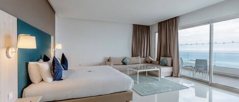 Quarto de hotel moderno com cama, sofá e varanda com vista.