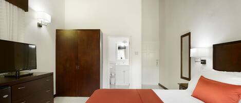 Quarto de hotel com cama, televisão, guarda-roupa e banheiro visível através de uma porta aberta.