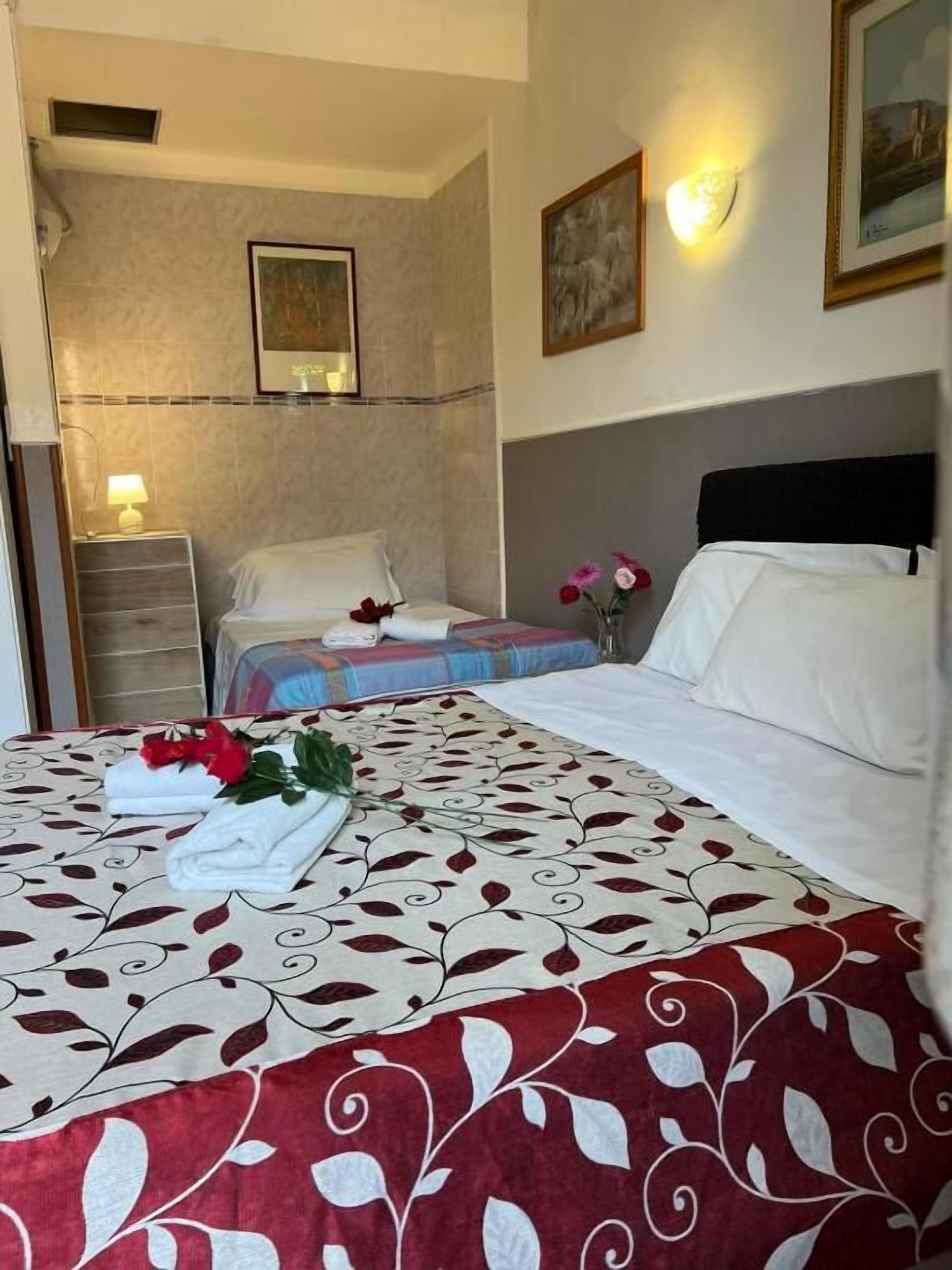 Quarto de hotel com uma cama grande, uma mesa de cabeceira, um criado-mudo e uma luminária fixada na parede.