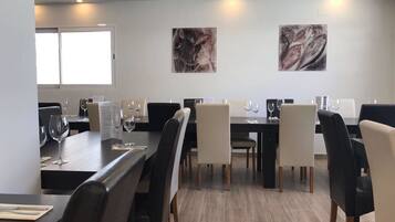 Uma área de jantar com uma mesa comprida, várias cadeiras e copos de vinho. Há duas obras de arte emolduradas na parede.