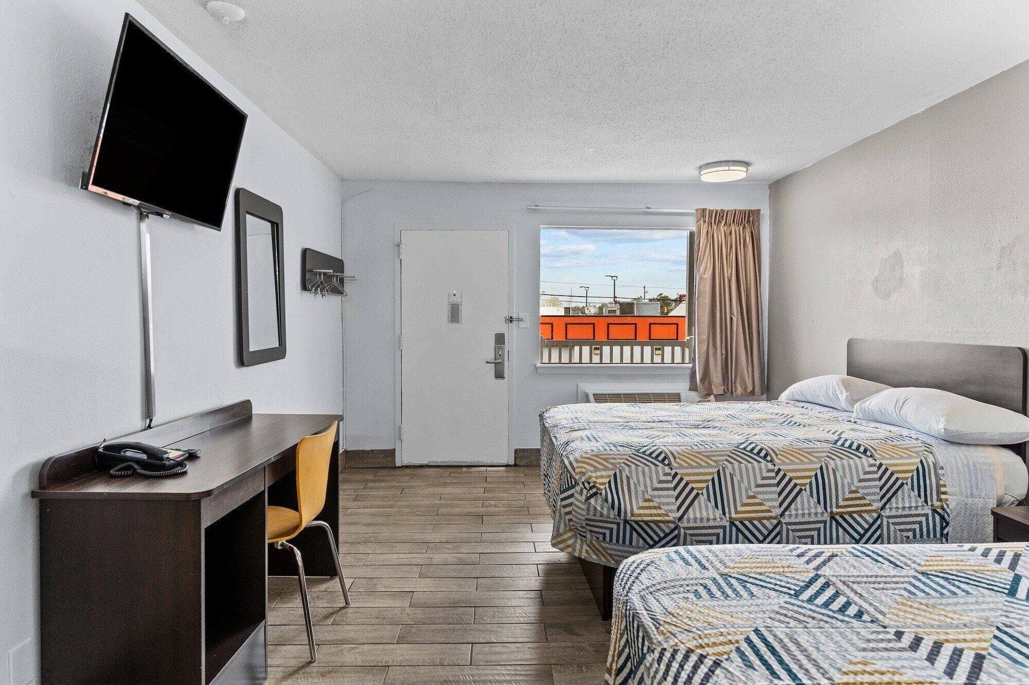 Quarto de hotel com duas camas, uma escrivaninha, uma cadeira, televisão e janela com vista para edifícios.