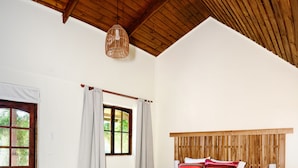 Quarto com teto de madeira, cama com manta listrada, cabeceira de madeira e janela com cortinas.