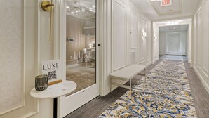 Um corredor com carpete estampado, um banco, uma placa indicando LUXE MED SPA e uma saída.