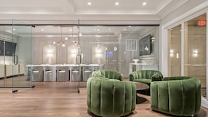 Um lobby moderno com divisória de vidro, assentos estofados em verde, um balcão de recepção e uma tela de televisão.