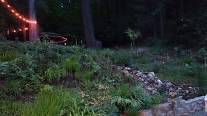 Um jardim ajardinado com muro de pedra, diversas plantas e luzes de fada.