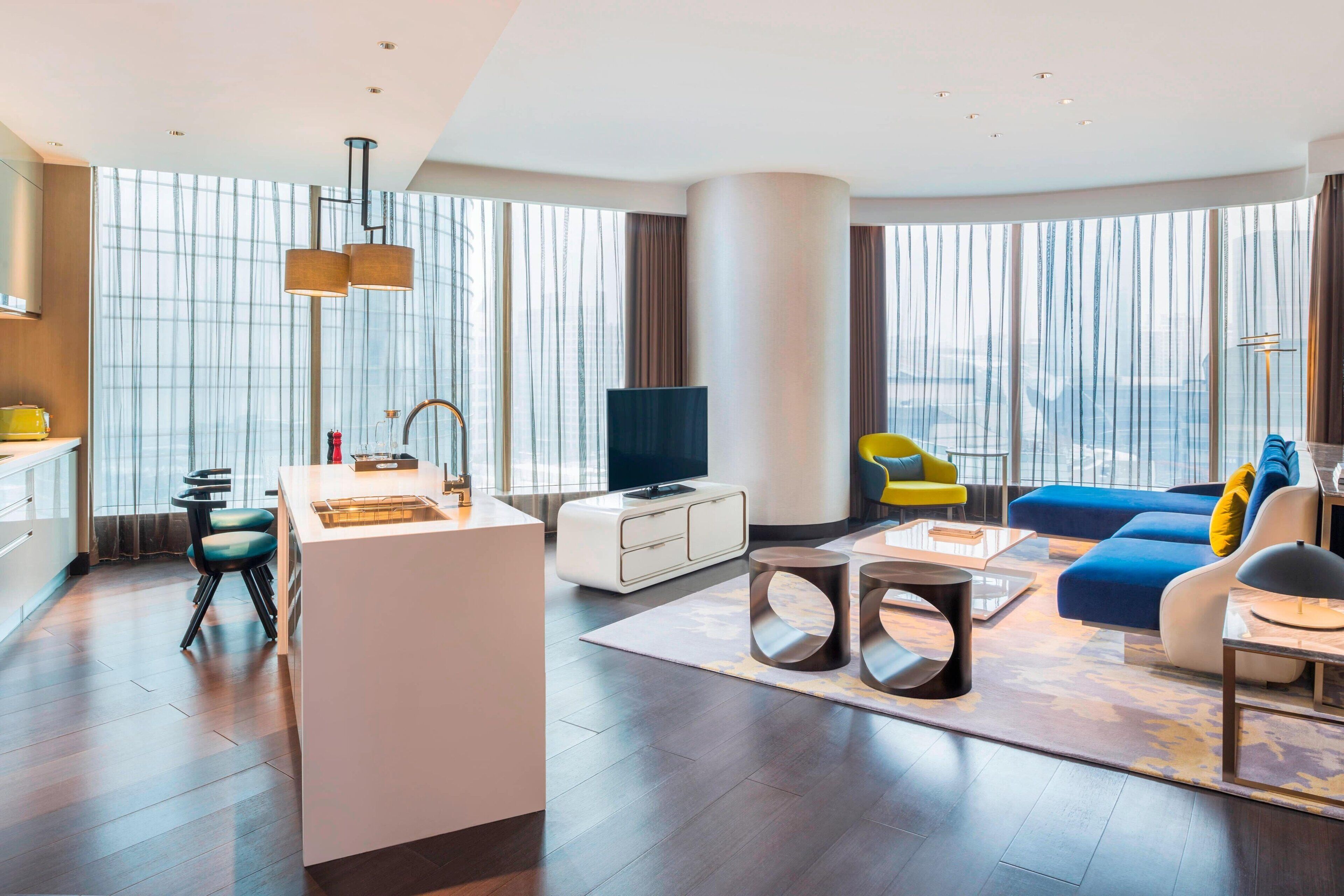Quarto de hotel moderno com área de estar, espaço para refeições e uma grande janela com vista para a cidade.