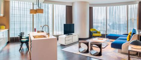 Quarto de hotel moderno com área de estar, espaço para refeições e uma grande janela com vista para a cidade.