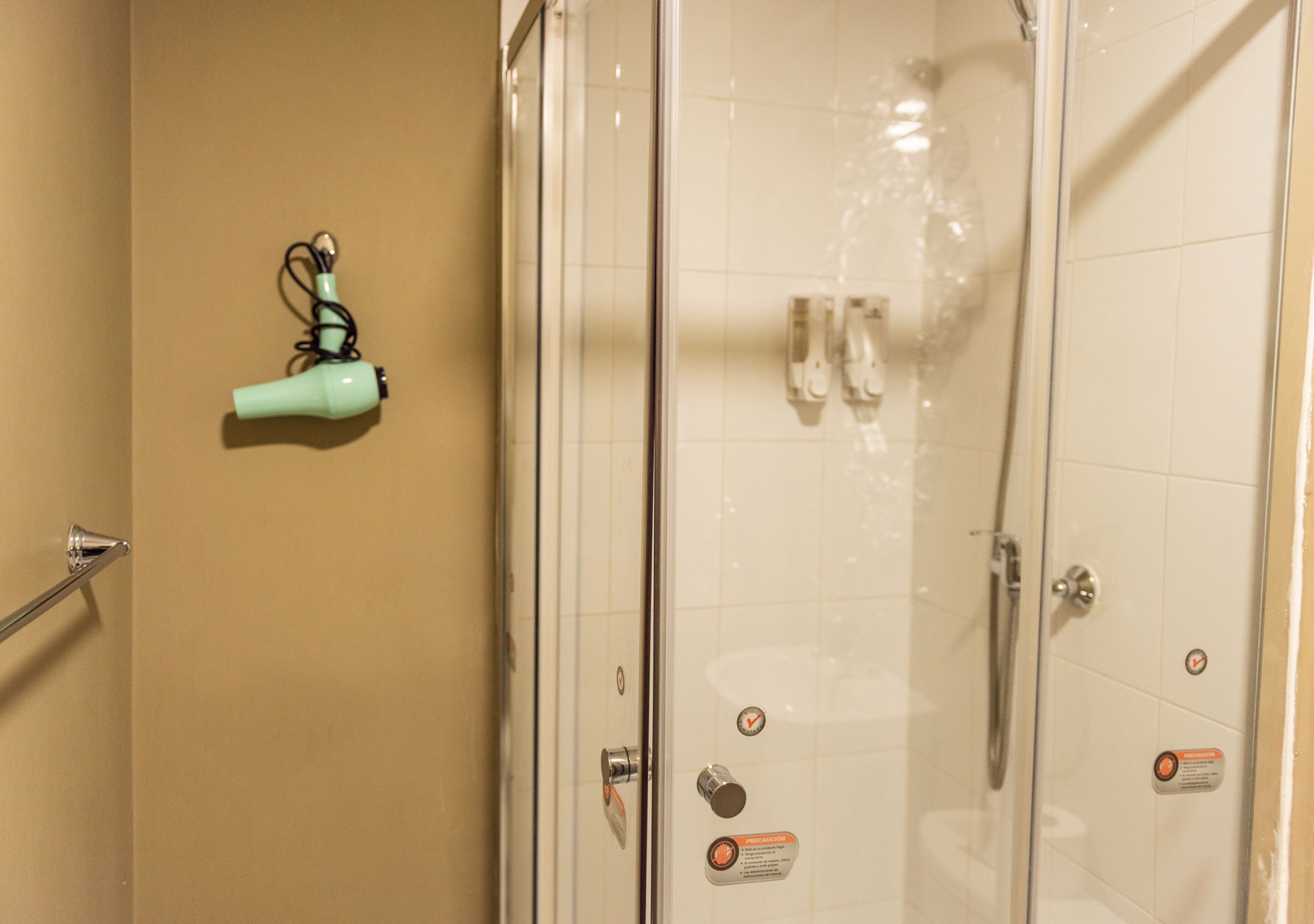 Uma casa de banho com cabine de chuveiro em vidro, um porta-toalhas e um secador de cabelo fixado na parede.