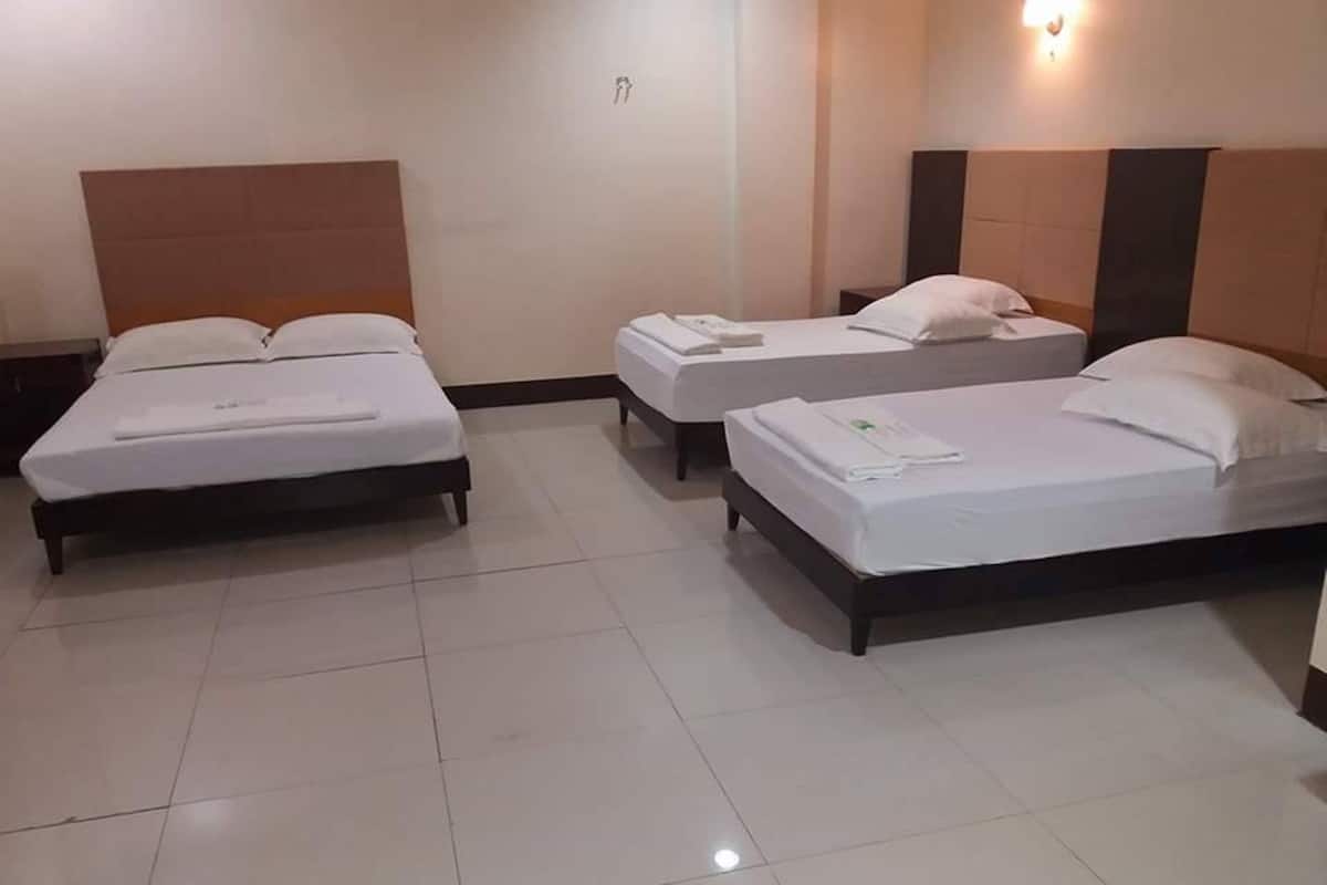 Quarto de hotel com três camas de solteiro, cada uma com cabeceira de madeira e roupa de cama branca.
