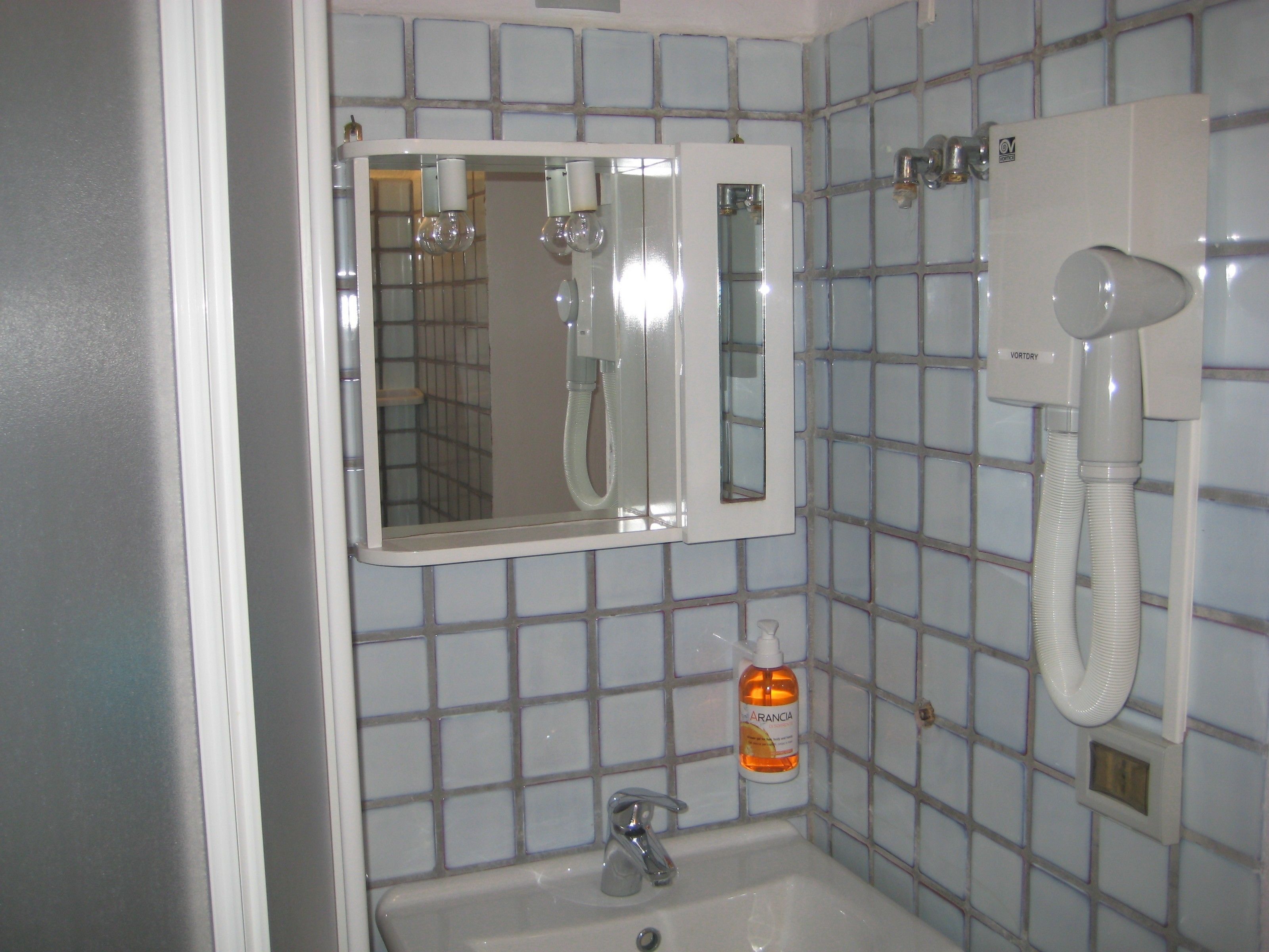 Casa de banho com lavatório, espelho e chuveiro manual fixo na parede.