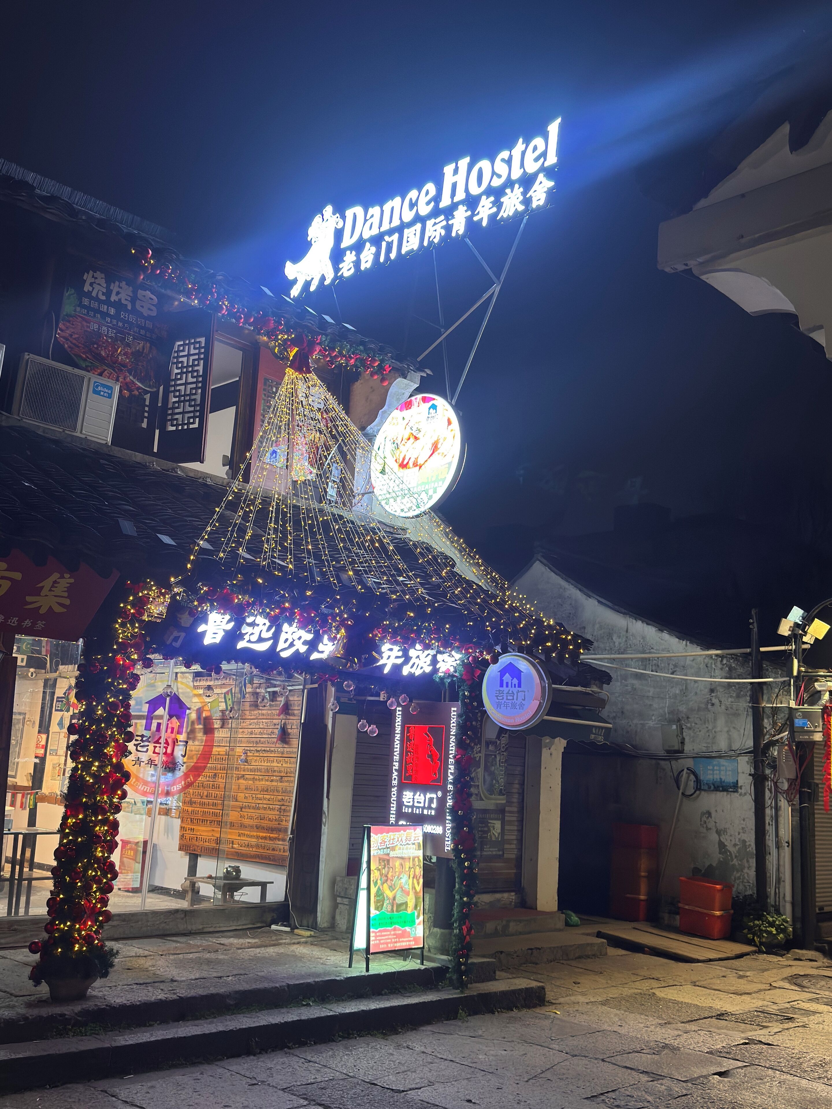 Um edifício com uma placa indicando "Dance Hostel" e um pinheiro de Natal decorado com luzes.