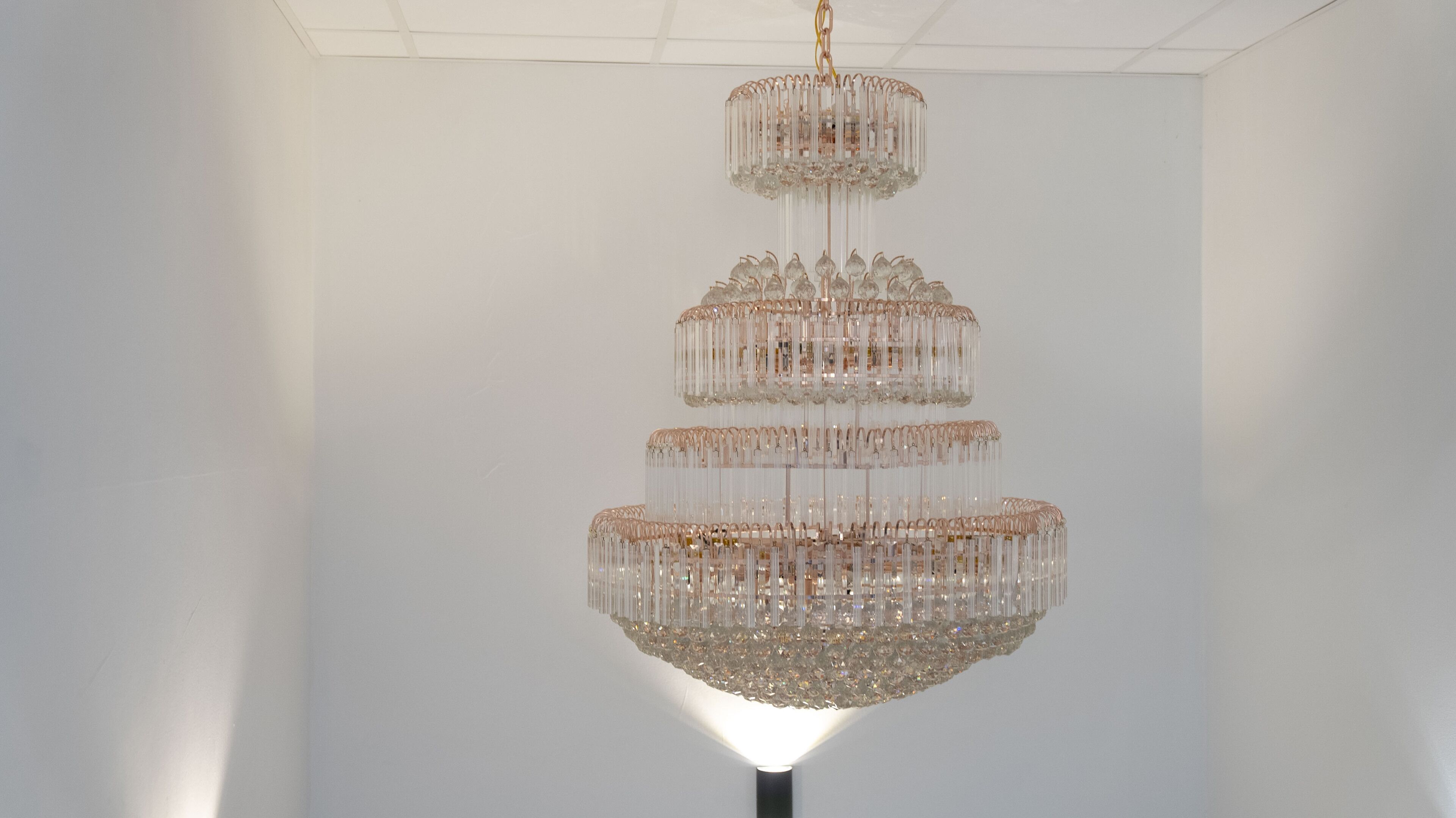 Um lustre de cristal em vários níveis pendurado no teto de um quarto com paredes brancas.