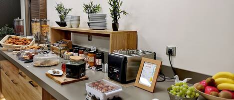 Disposição de buffet com diversos alimentos, uma máquina de café e um dispensador de suco.
