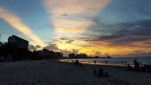 Uma praia com edifícios ao fundo durante o pôr do sol.