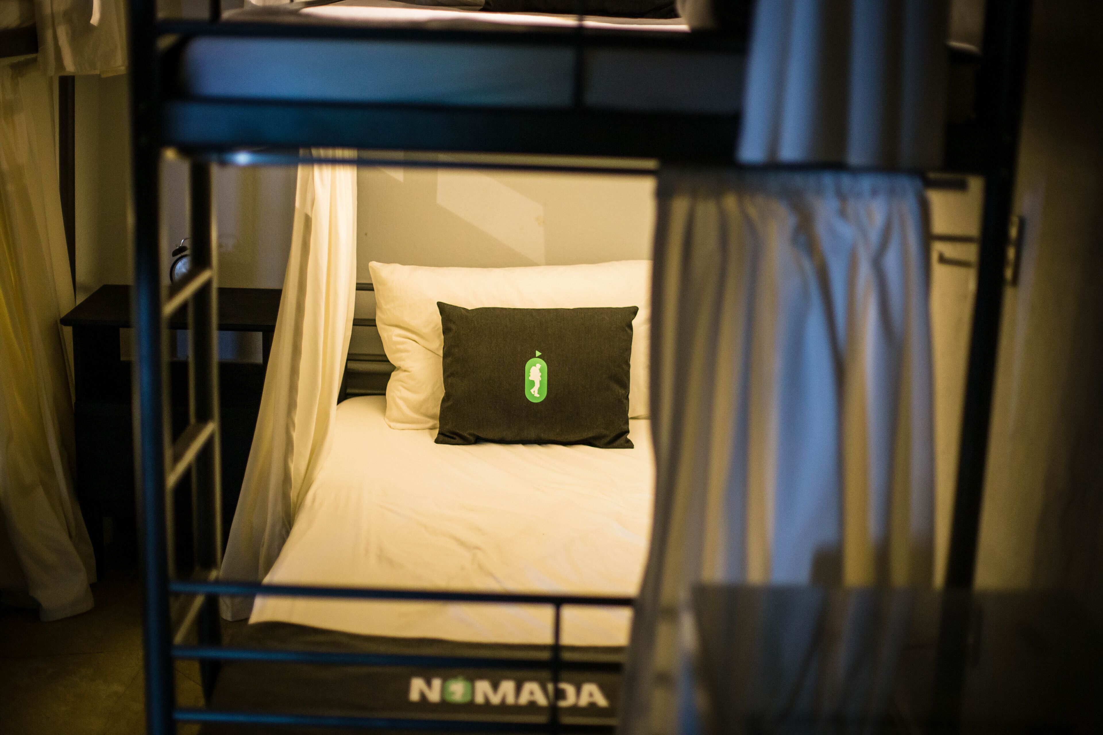Uma cama beliche com colchão branco e travesseiro preto com logotipo verde.