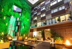 Interior moderno de hotel com parede verde, piscina interior e vários andares com varandas.