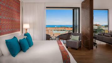 Quarto de hotel com uma cama grande, um sofá, uma cadeira e vista para o mar.