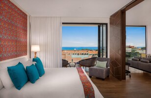 Quarto de hotel com uma cama grande, um sofá, uma cadeira e vista para o mar.