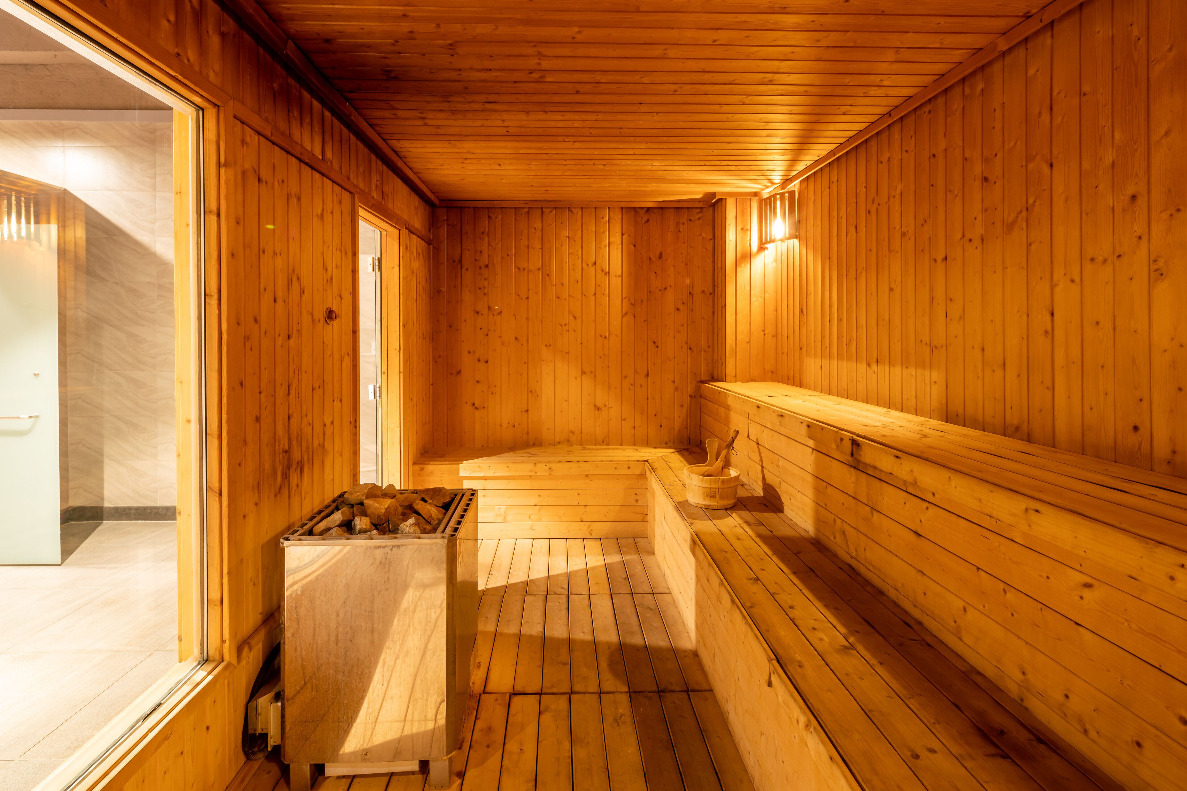 Uma sala de sauna com paredes e bancos de madeira, um aquecedor de banco e uma bacia de pedra.