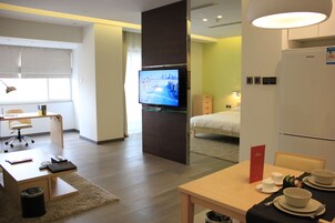 Quarto de hotel com uma cama, uma mesa de escritório com um computador, uma televisão e um espaço de refeições com mesa posta para dois.