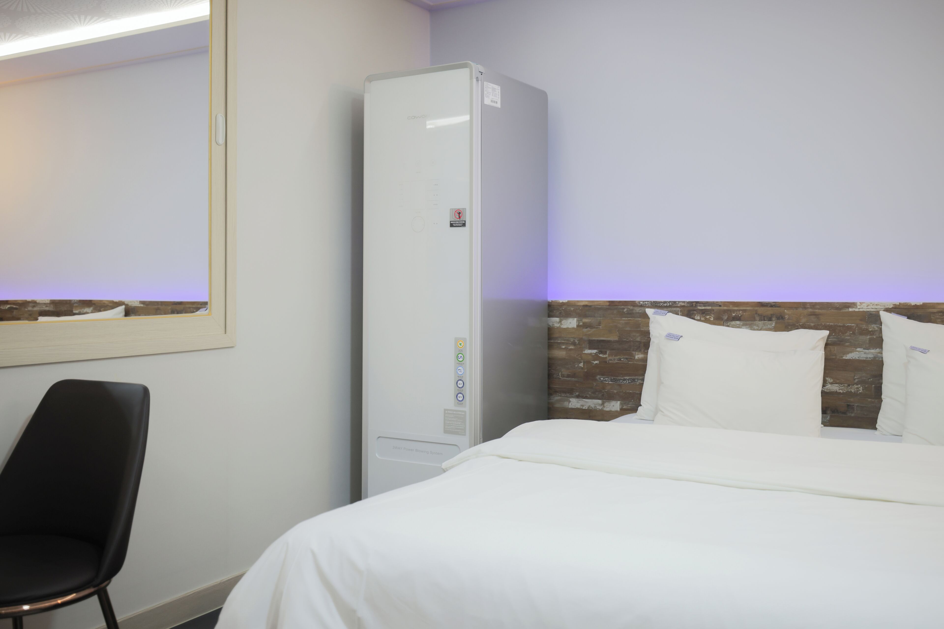 Quarto de hotel com uma cama, uma cadeira, parede branca e parede de destaque em tijolo, além de um ar condicionado branco.