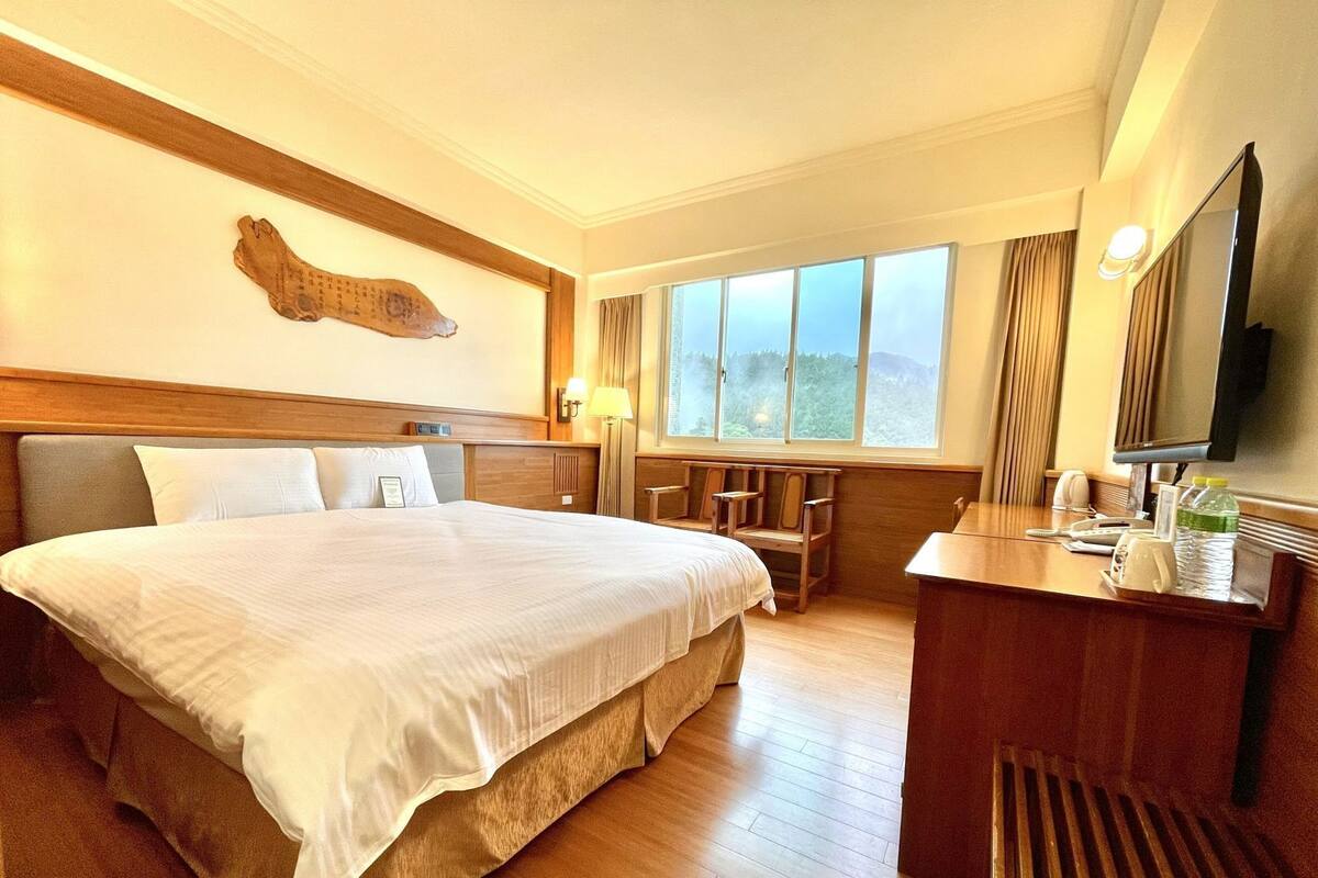 Quarto de hotel com uma cama grande, uma escrivaninha com cadeira, televisão e janela com vista.