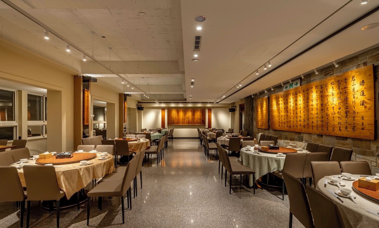 Restaurante com mesas redondas, cadeiras e uma parede com caligrafia.
