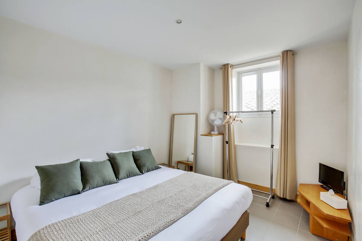 Quarto de hotel com uma cama grande, mesa de cabeceira com abajur, televisão e janela com cortinas.