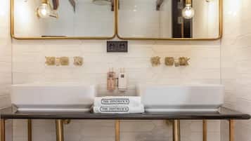 Casa de banho com duas pias, um espelho com iluminação e um porta-toalhas com toalhas da marca Hendrick's.