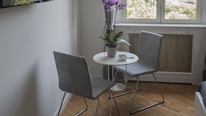 Quarto moderno com mesa de jantar, duas cadeiras, planta em vaso e vista para a cidade através de uma janela.