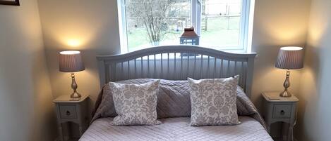 Uma cama bem arrumada com cobertura acolchoada, duas luminárias de cabeceira e uma janela com vista para o exterior.