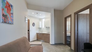 Uma sala de estar moderna com sofá, cozinha ao fundo e uma porta que dá para outro espaço.