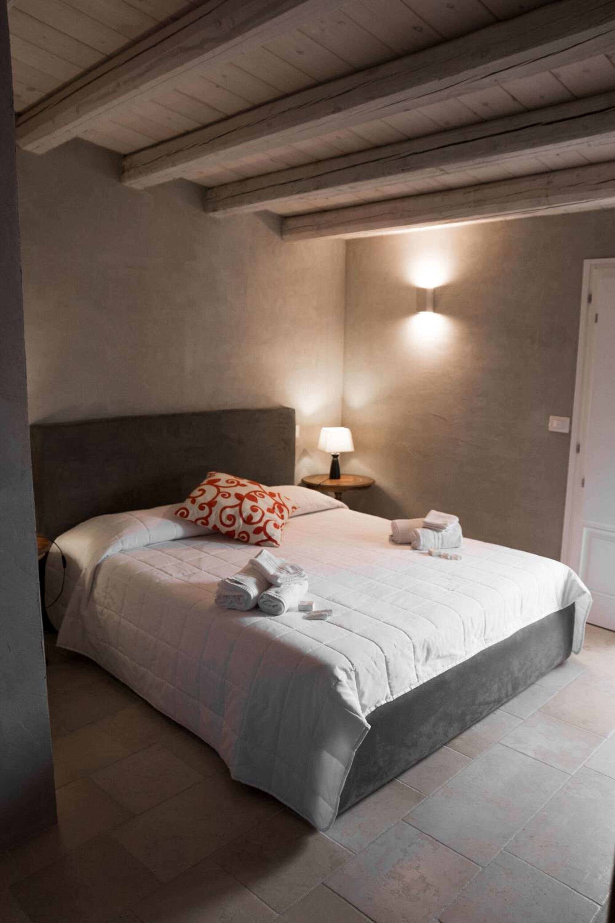 Um quarto com cama, mesa de cabeceira, abajur e porta.