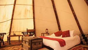 Interior acolhedor de uma tenda com uma cama, móveis de madeira e um candeeiro.