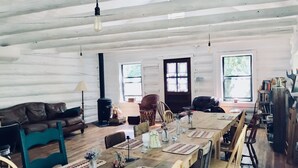 Interior rústico de uma cabana, com uma longa mesa de jantar, paredes de madeira e uma lareira.