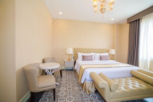Quarto de hotel com uma cama grande, duas mesas de cabeceira, uma cadeira e uma mesinha.