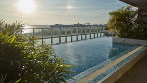 Piscina com barreira de vidro e vista para o mar e edifícios ao fundo.