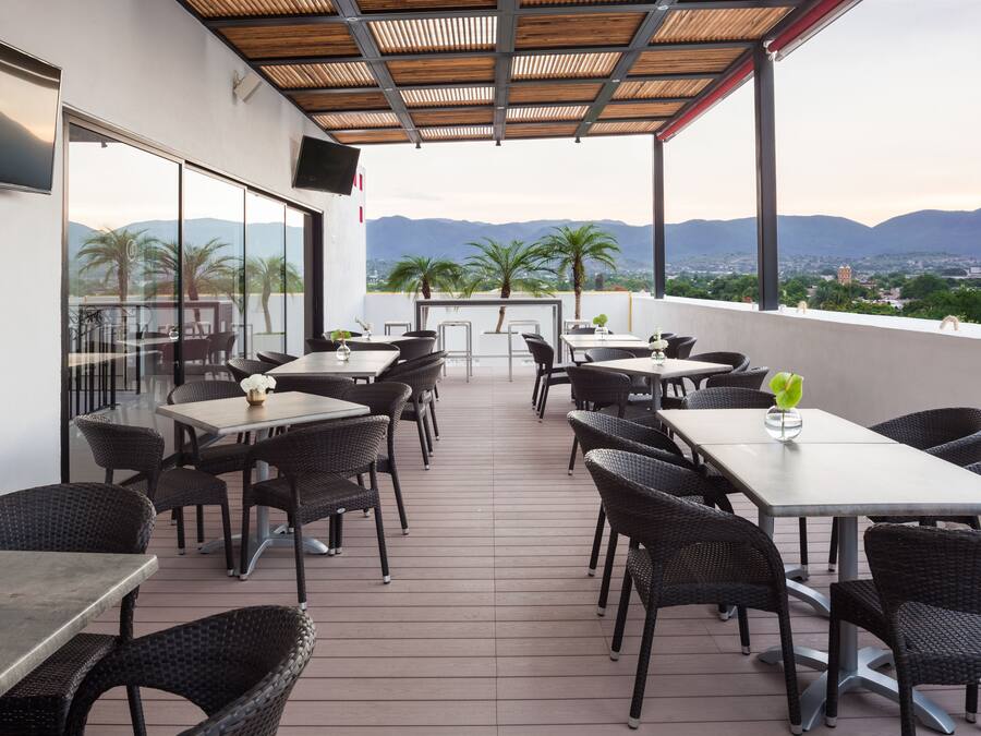 Terraço com mesas e cadeiras, vista para a cidade e montanhas.