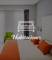 Quarto de hotel com uma cama, uma poltrona verde e uma mesa de cabeceira com luminária.