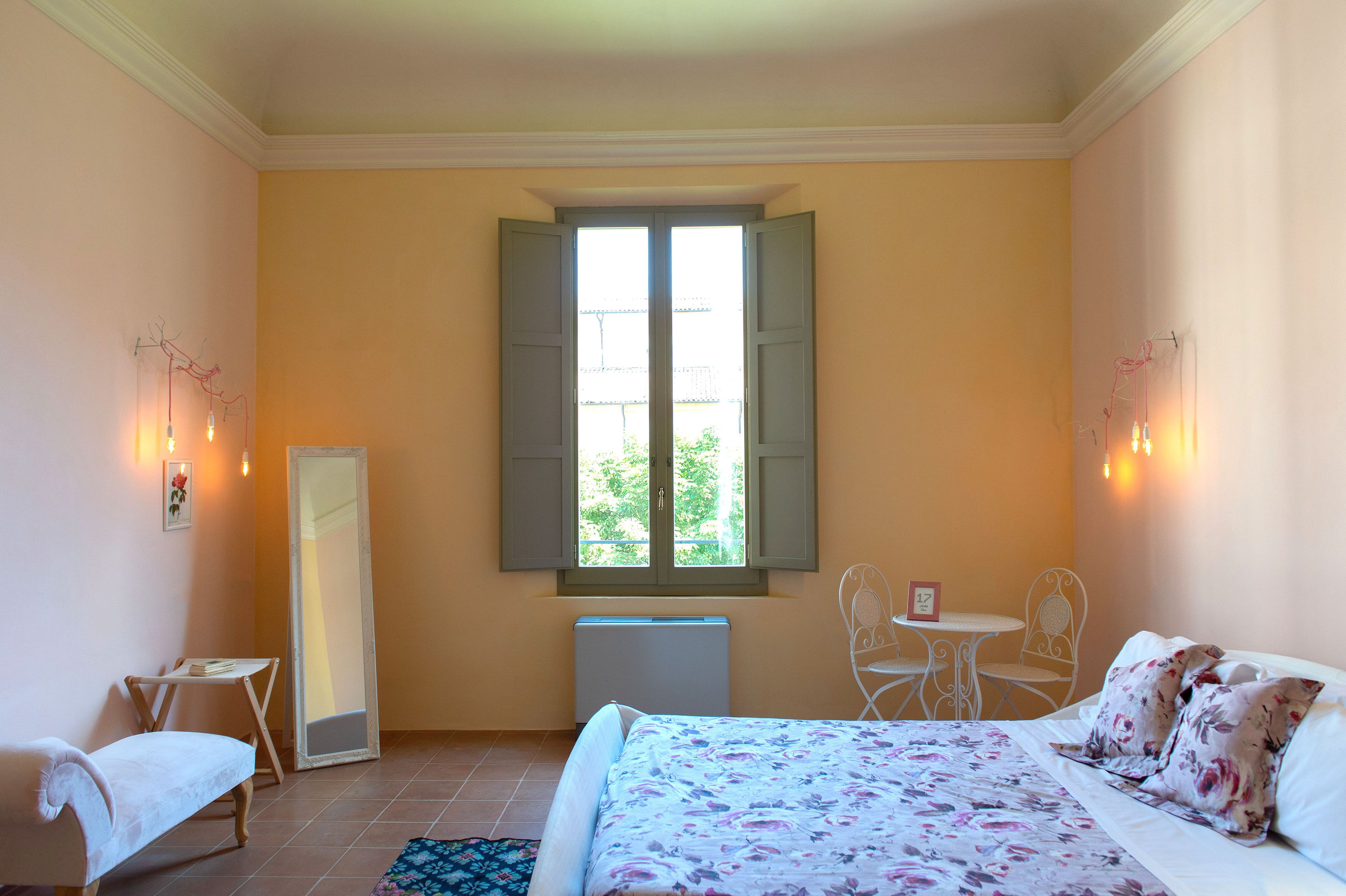 Quarto com cama, cadeira, mesinha e espelho.