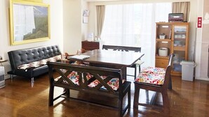 Uma sala de estar com sofá, mesa de jantar e cadeiras, armário de madeira e uma janela grande com cortinas.