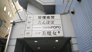 Uma placa com texto em japonês indicando diferentes andares e nomes, provavelmente de um edifício ou hotel.