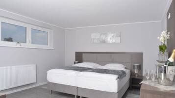 Quarto moderno com cama, mesas de cabeceira, radiador, janela e um objeto decorativo na parede.