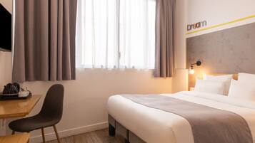 Quarto de hotel com cama, escrivaninha, cadeira e janela com cortinas.