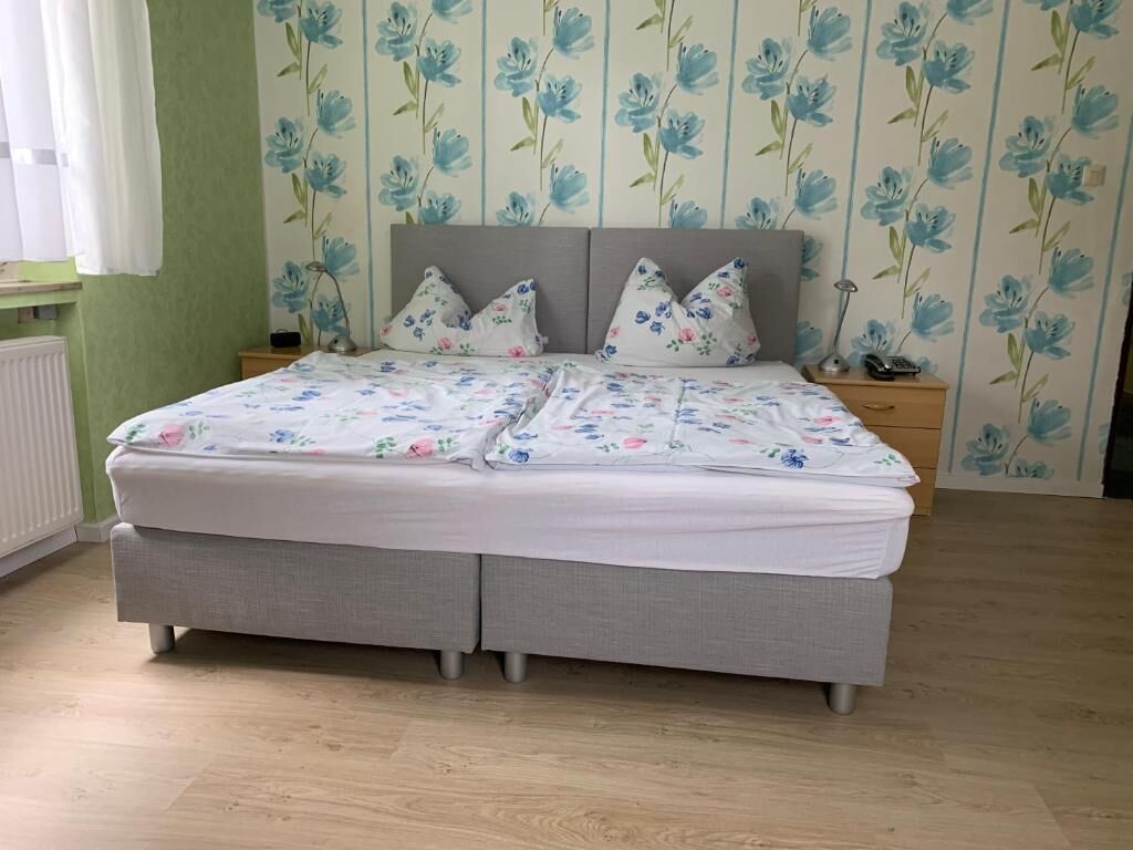 Quarto com cama, duas mesas de cabeceira e papel de parede floral.